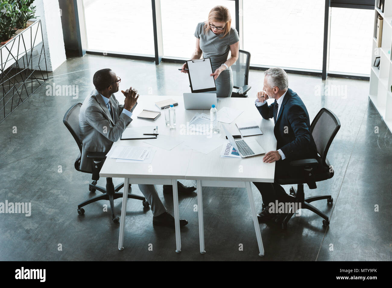 high angle view of businesswoman showing blank clipboard to multiethnic ...