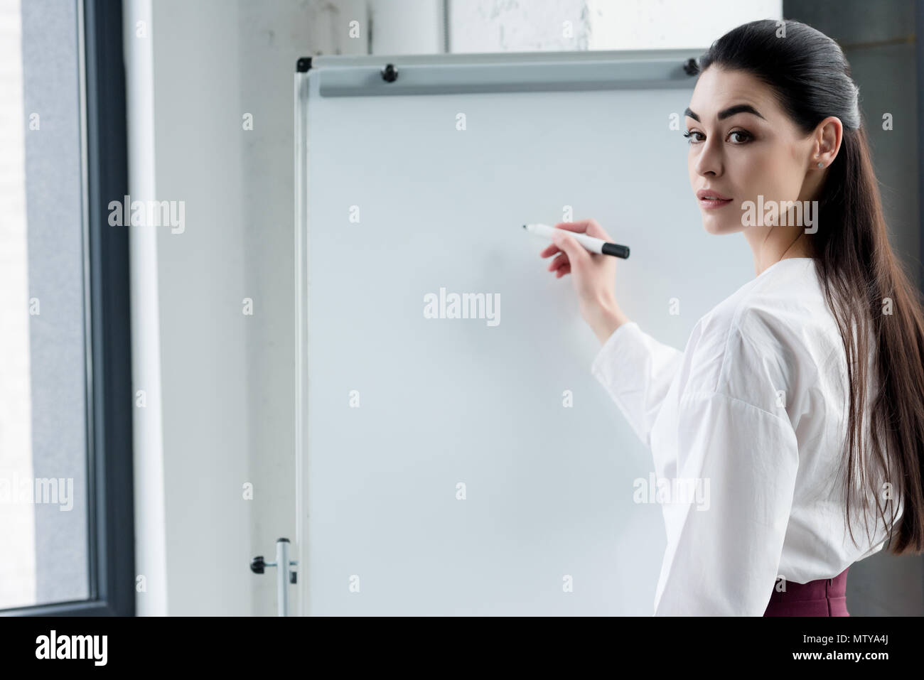 beautiful young businesswoman writing on blank whiteboard in office ...