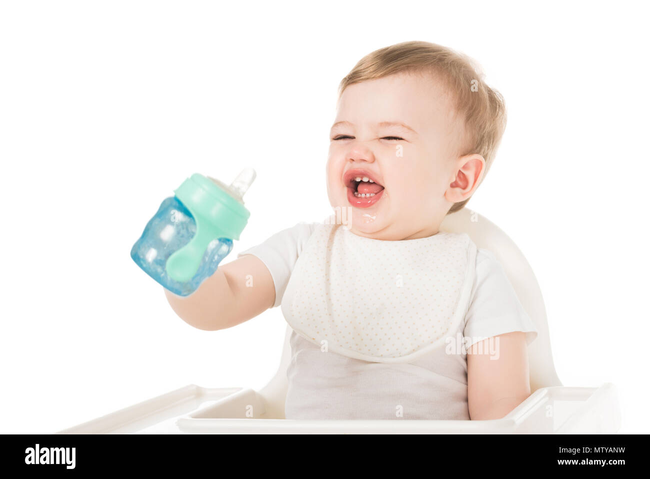 crying little boy in bib holding baby cup and sitting in highchair ...