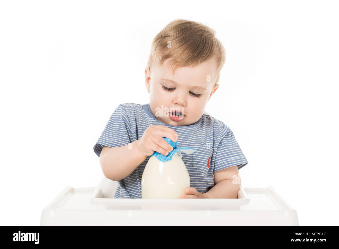 little boy trying to open bottle of milk and sitting in highchair ...