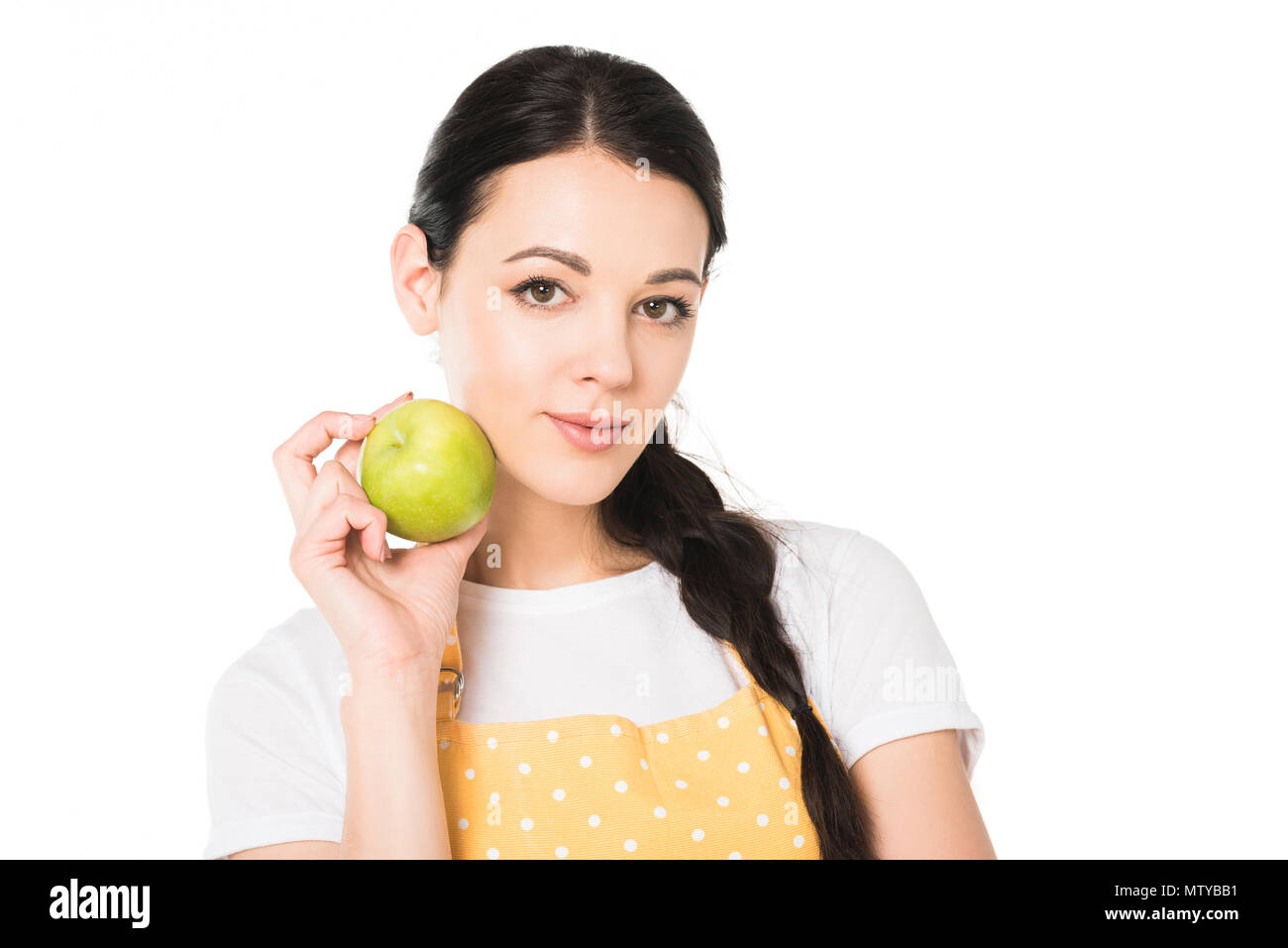 young woman in apron holding apple near cheek isolated on white ...