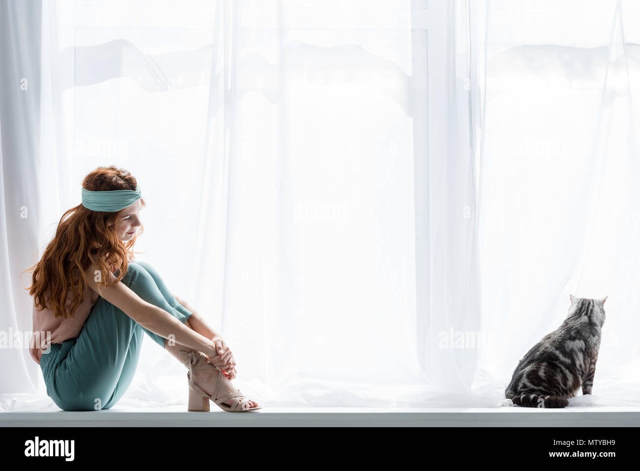 attractive young woman sitting on windowsill with cute tabby cat Stock ...