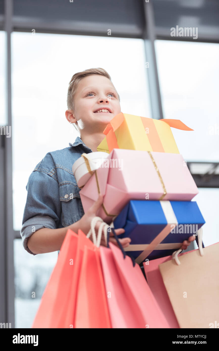 happy boy holding colored boxes with paper bags in hands at shop ...