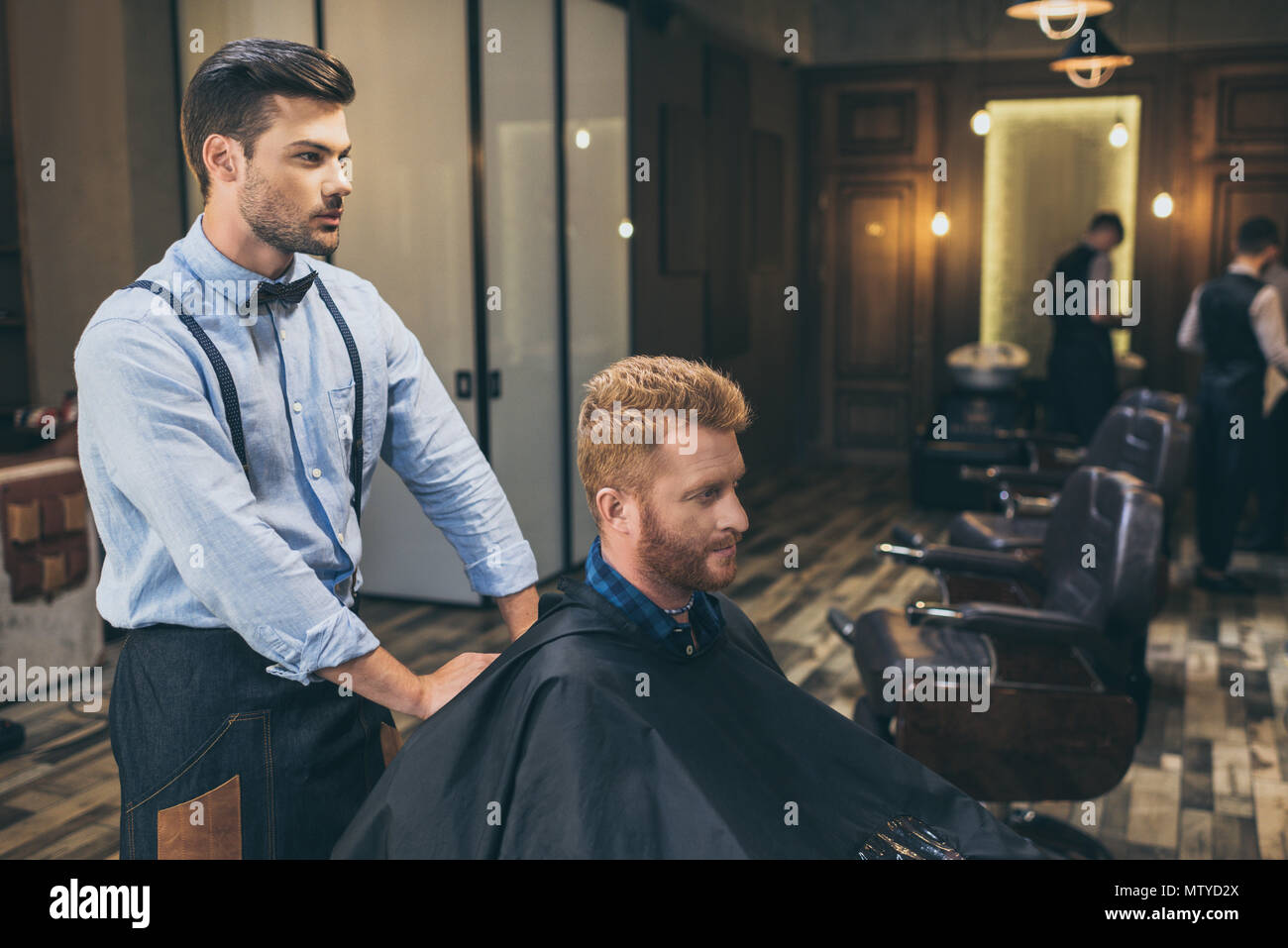 Stylish young barber standing behind customer that sitting in barber ...