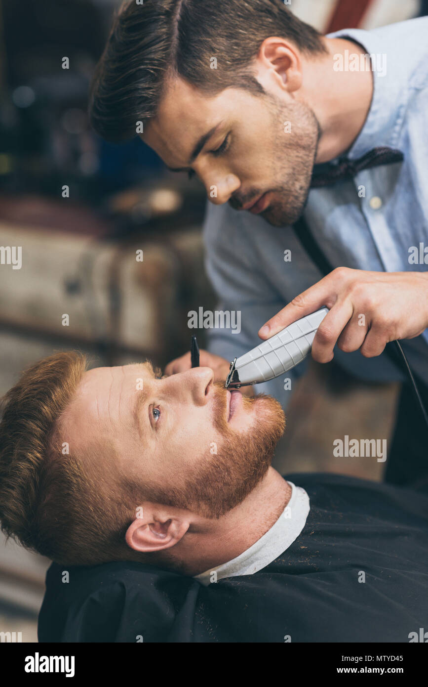 Male barber trimming customers beard in barber shop Stock Photo - Alamy