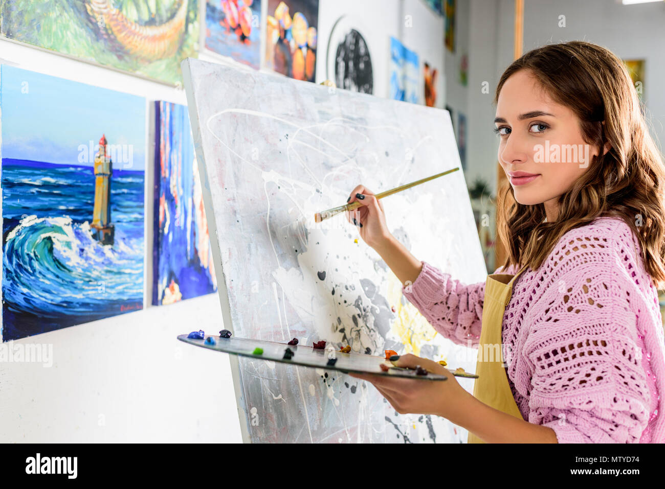 beautiful female artist looking at camera during painting in workshop ...