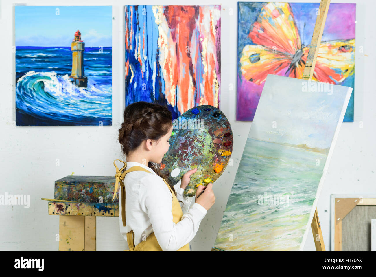 side view of kid taking paint from palette in workshop of art school ...