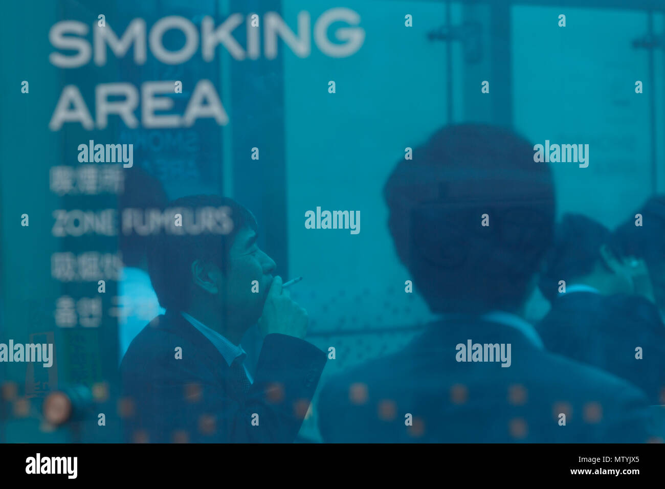 People smoke in a designated smoking area outside Shinjuku Station on ...