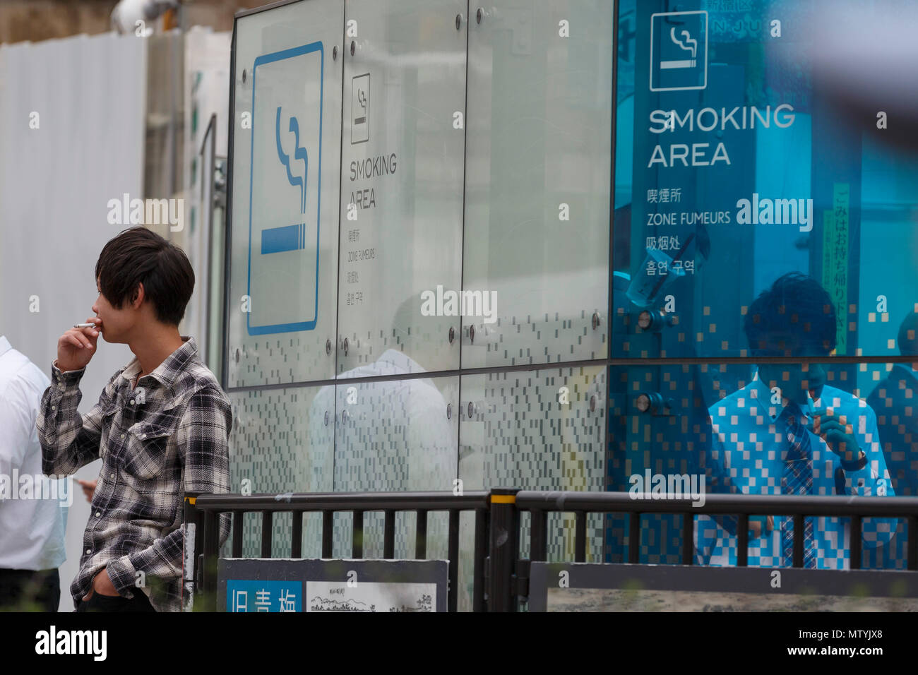 People smoke in a designated smoking area outside Shinjuku Station on ...