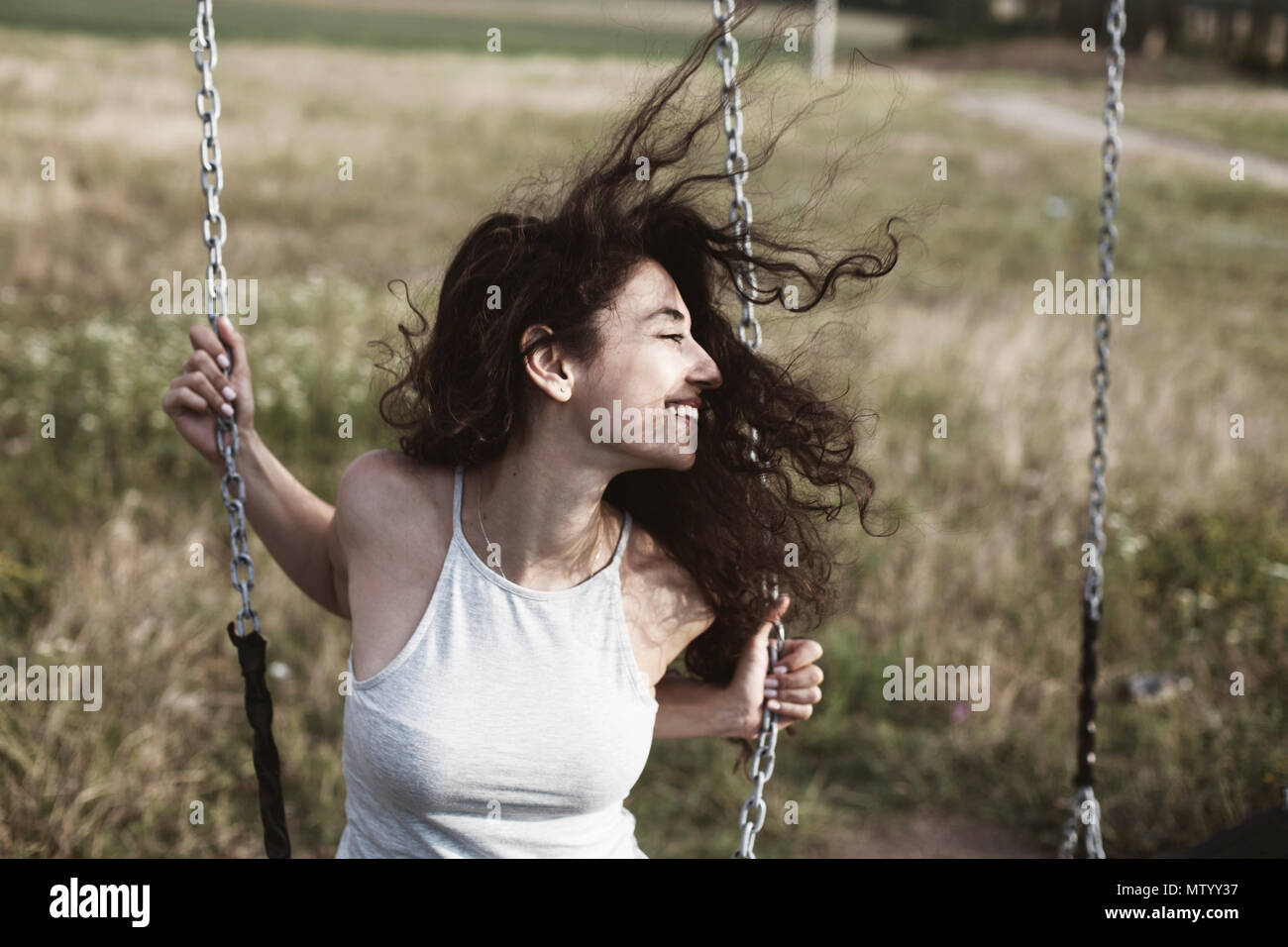 Woman with windswept hair sitting on a swing Stock Photo - Alamy
