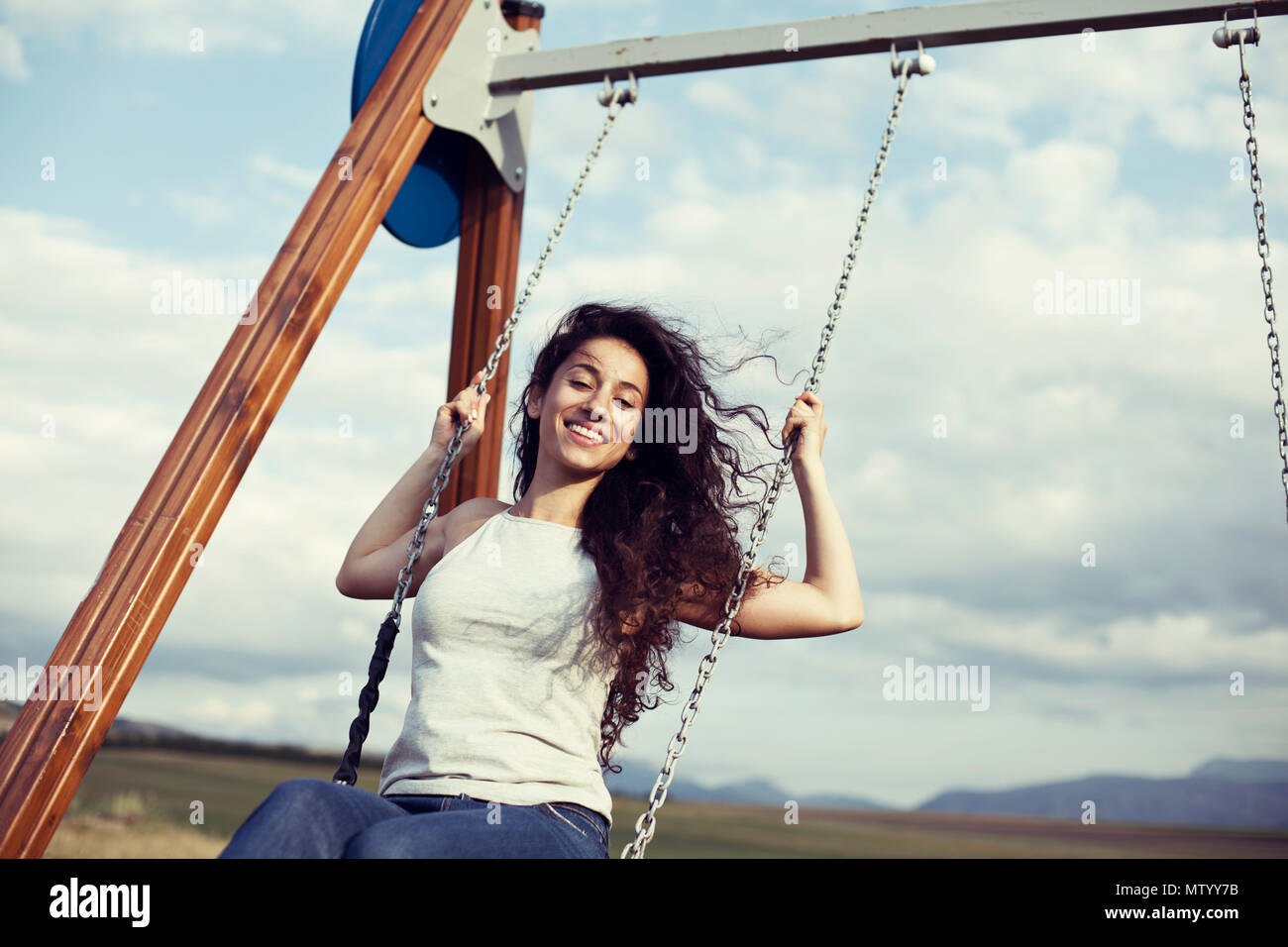 Woman with windswept hair sitting on a swing Stock Photo - Alamy