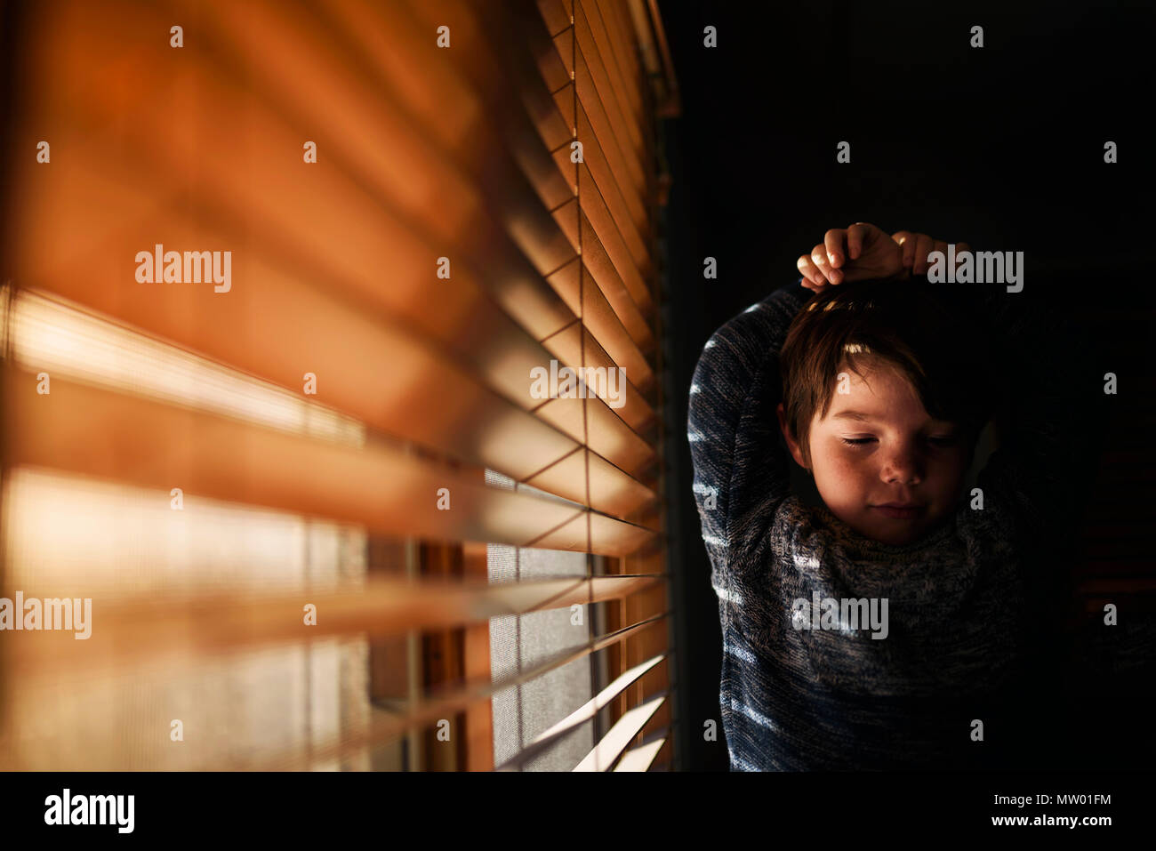 Tired Boy standing by a window stretching Stock Photo - Alamy