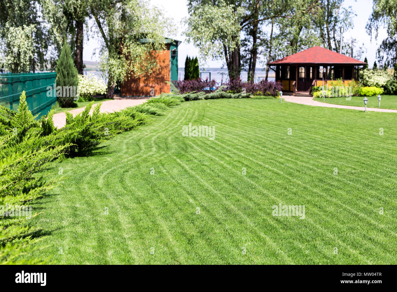 Freshly mowed rows of green lawn at country residence with summerhouse ...