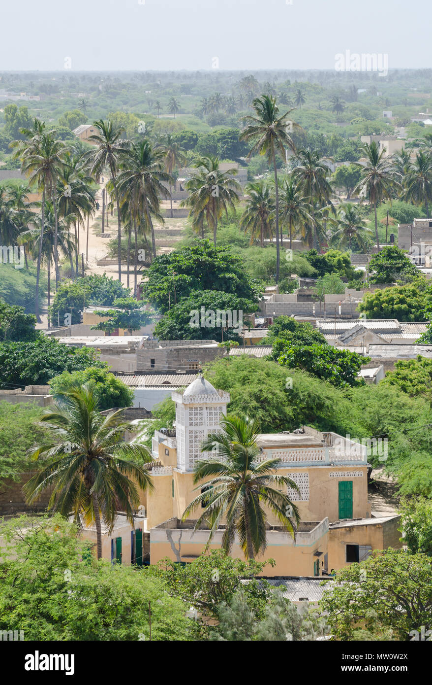 Simple yellow mosque surrounded by green vegetation and palm trees at ...
