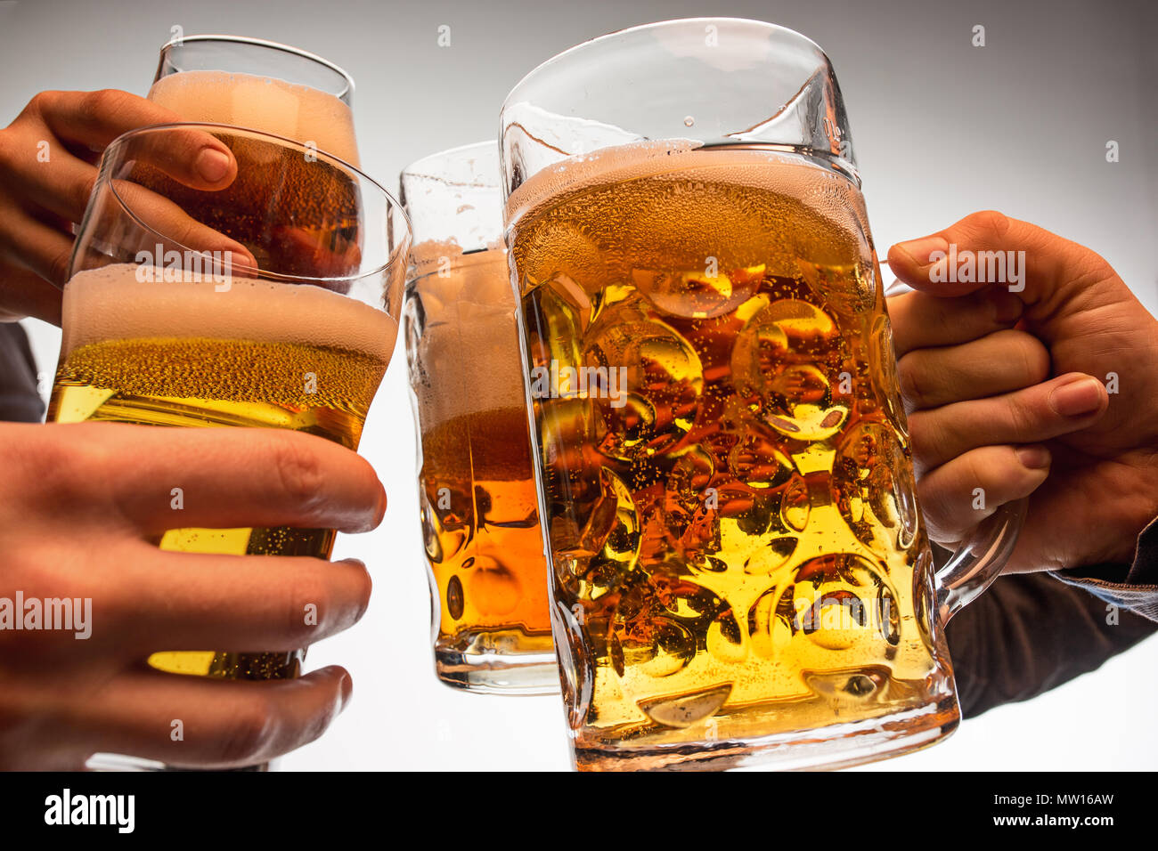 hands with mugs of beer toasting creating splash isolated on white ...