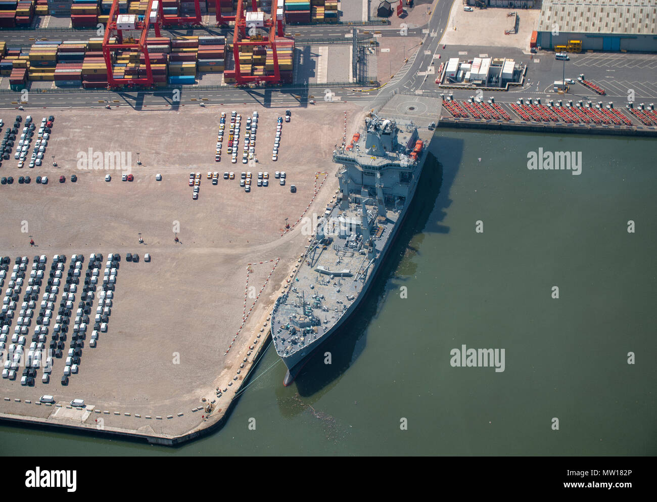 Aerial photo of naval ship in port with parked lines of cars and cranes ...