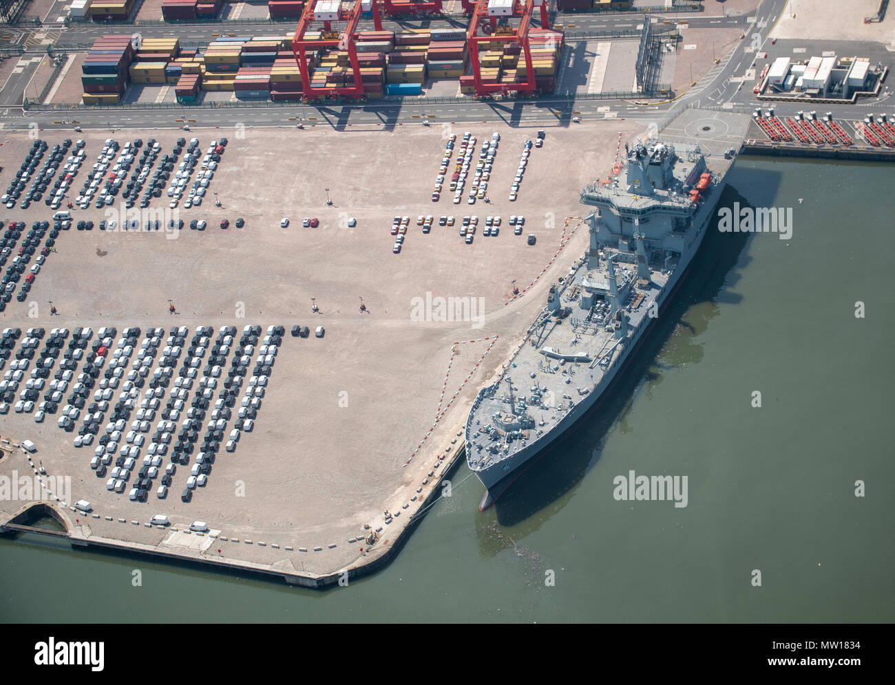 Aerial photo of naval ship in port with parked lines of cars and cranes ...