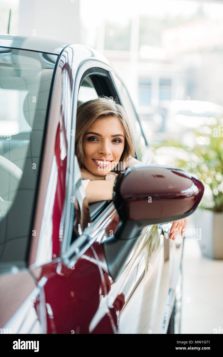 Happy smiling female customer sitting in a red car in showroom and ...