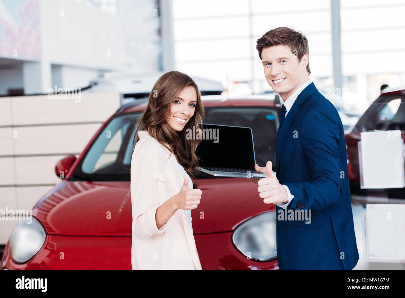 Customer and manager showing thumbs up to the camera in car showroom ...