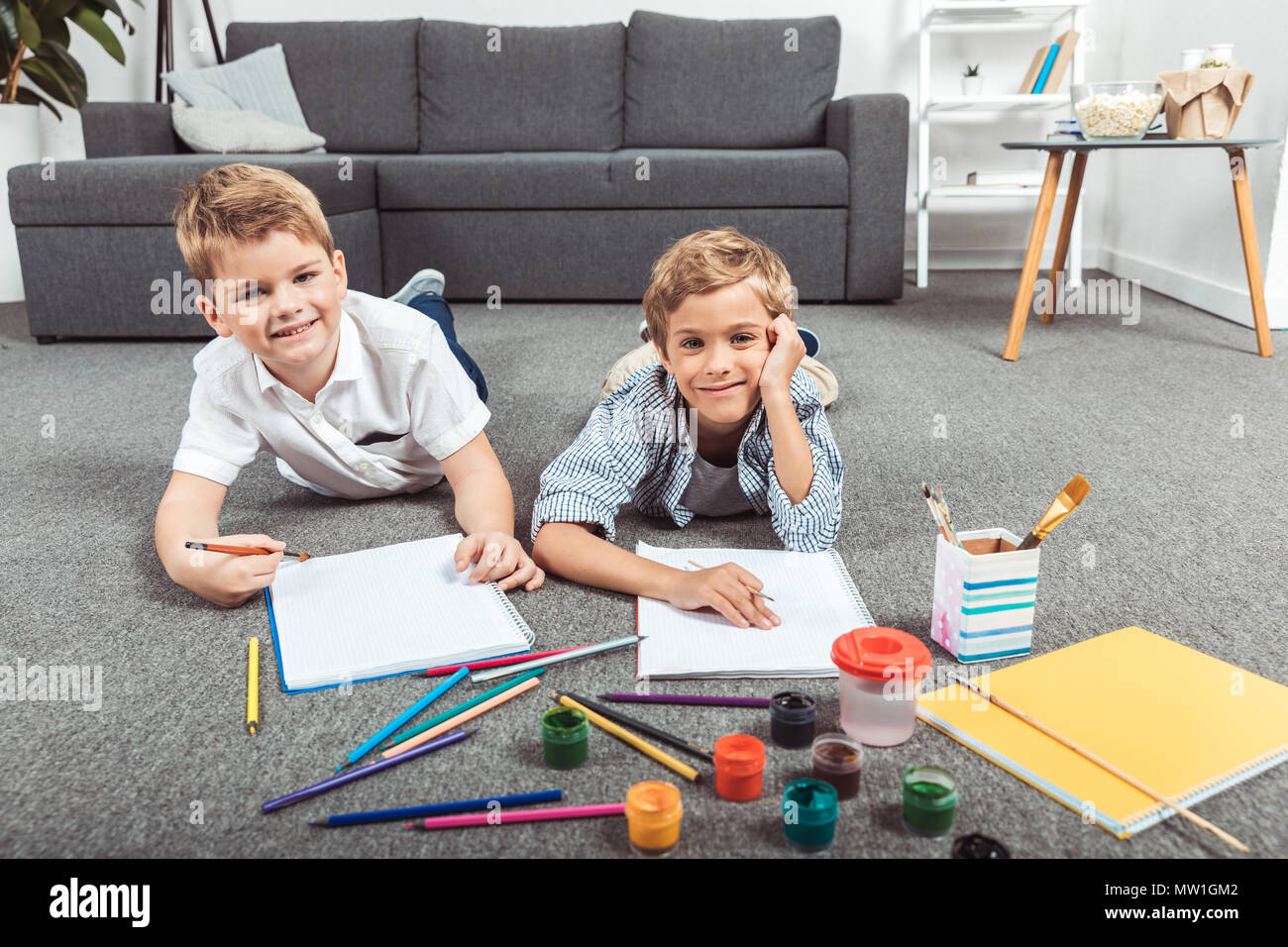 adorable little boys drawing together and smiling at camera at home ...