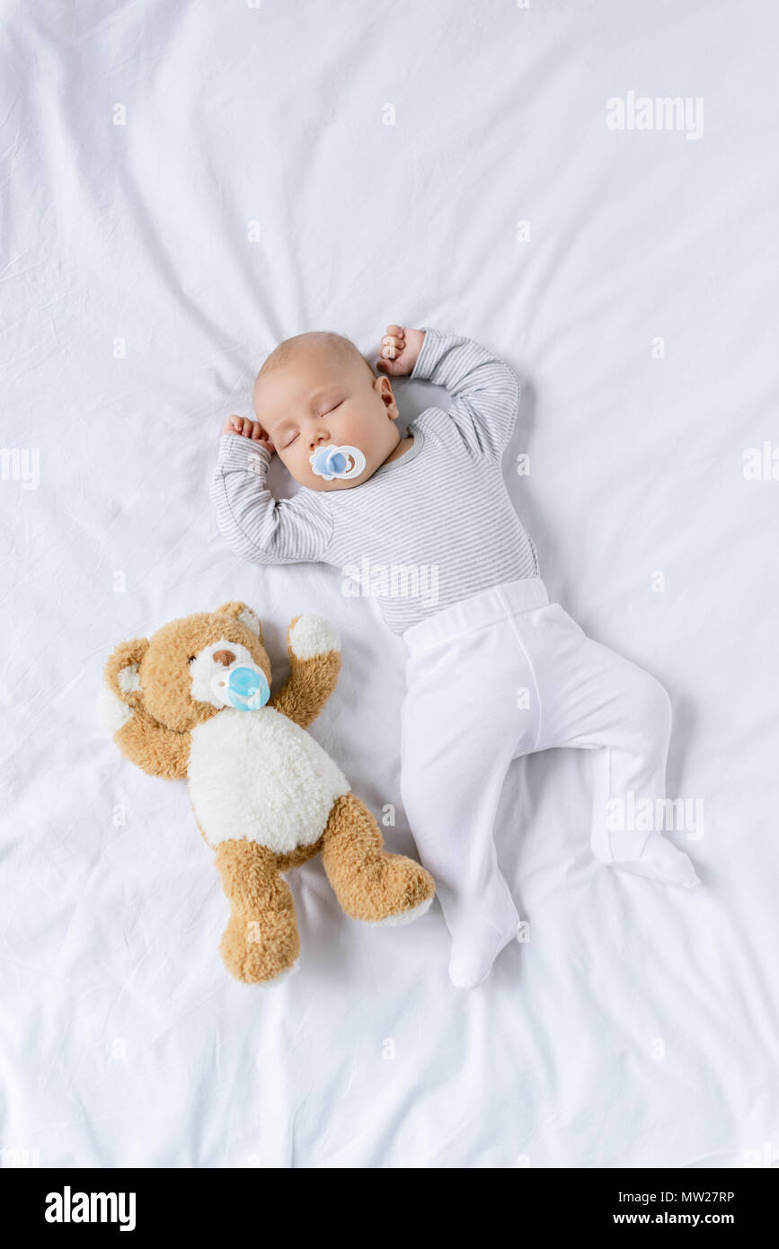 overhead view of cute baby with pacifier sleeping on bed with teddy ...
