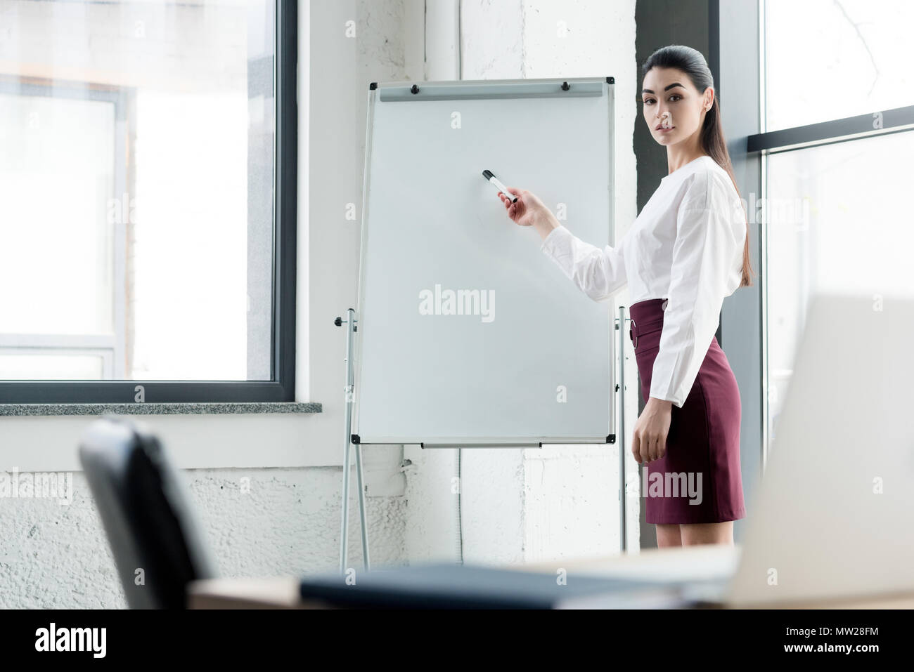 beautiful young businesswoman pointing at whiteboard and looking at ...