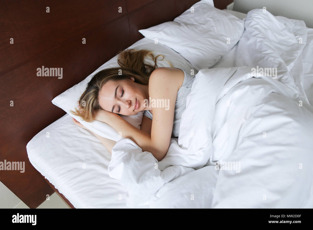 Young nice girl sleeping in morning on wooden bed with white linens ...
