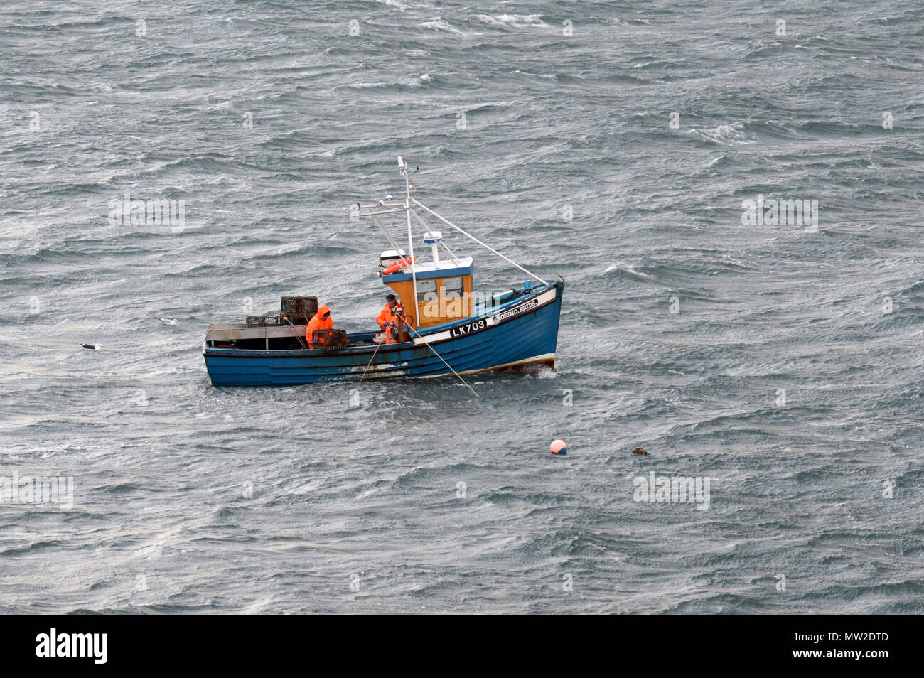 Small fishing boat at sea with 2 crew aboard picking up lobster baskets ...