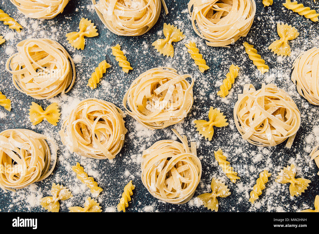Various uncooked pasta scattered in flour on black background Stock ...