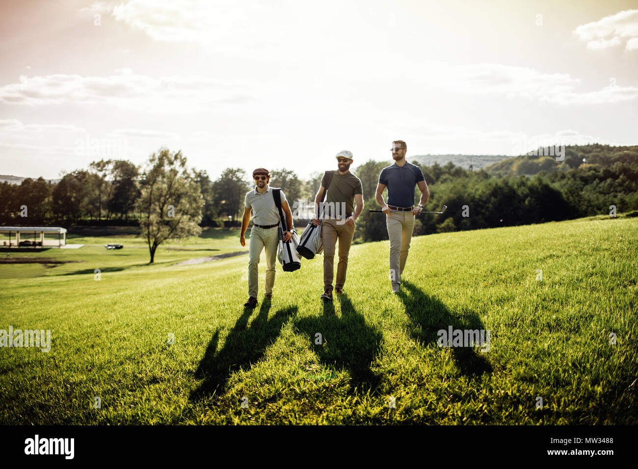 Three smiling men in sunglasses holding golf clubs outdoors Stock Photo ...