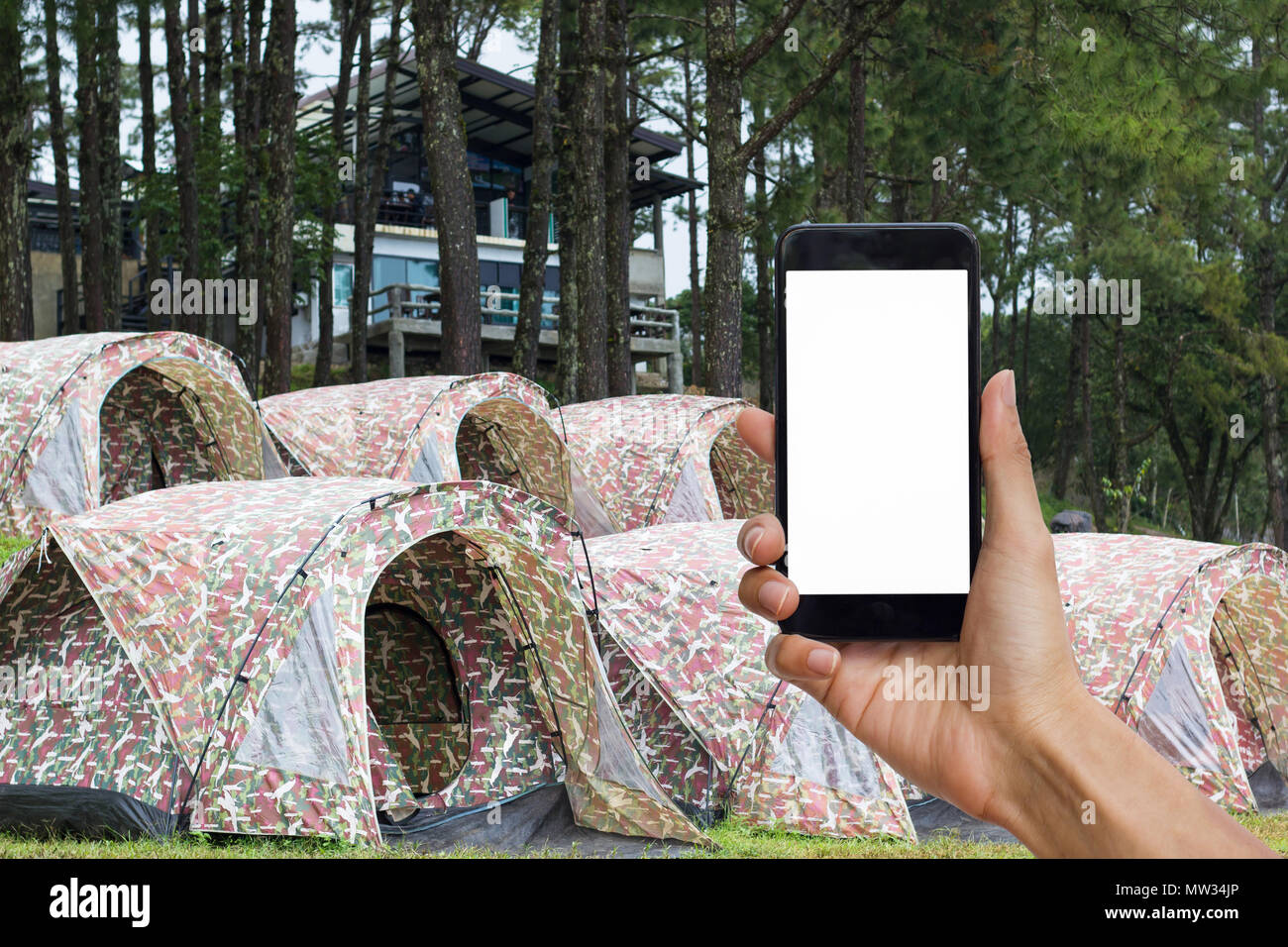 Hand holding black smartphone with white screen for mock up on camping ...