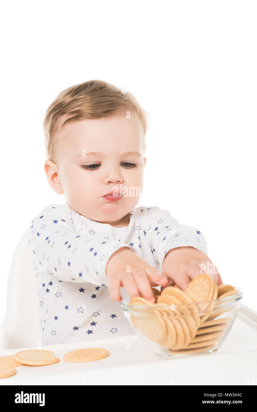 little boy taking cookies from bowl and sitting in highchair isolated ...