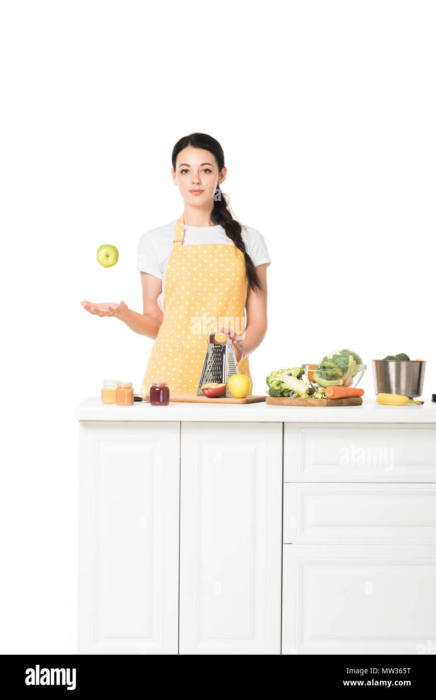 young woman throwing up apple at tabletop with fruits and vegetables ...