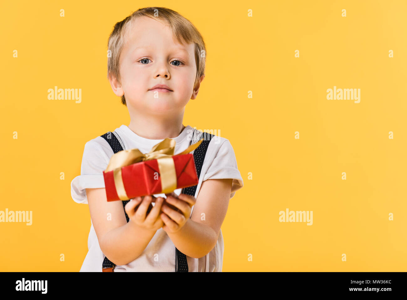 selective focus of little boy with wrapped present isolated on yellow ...