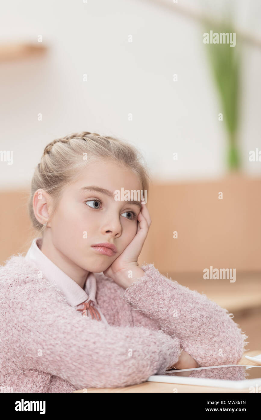 bored child sitting at table with digital tablet and looking away Stock ...