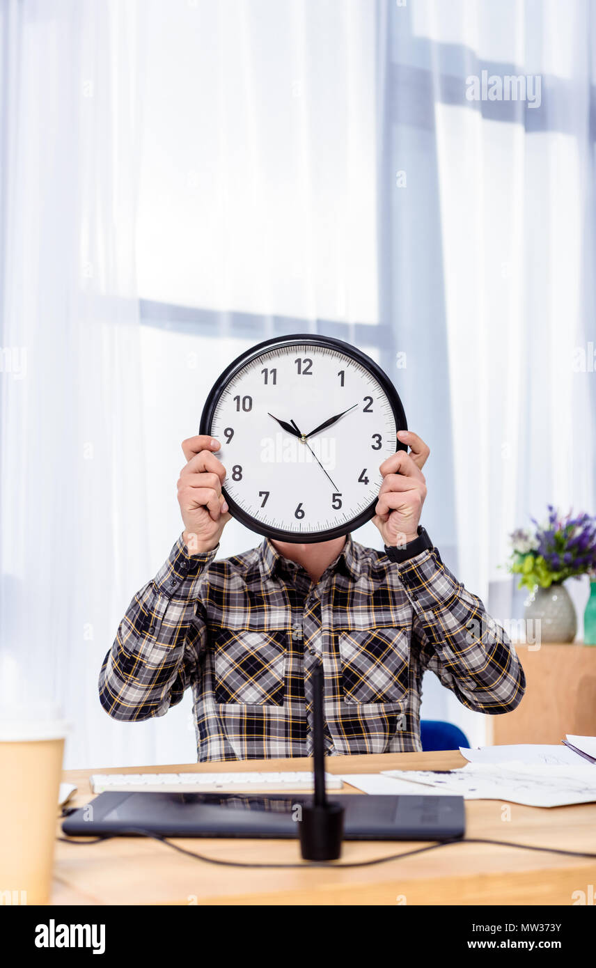 Man holding clock over face while sitting at working table Stock Photo ...