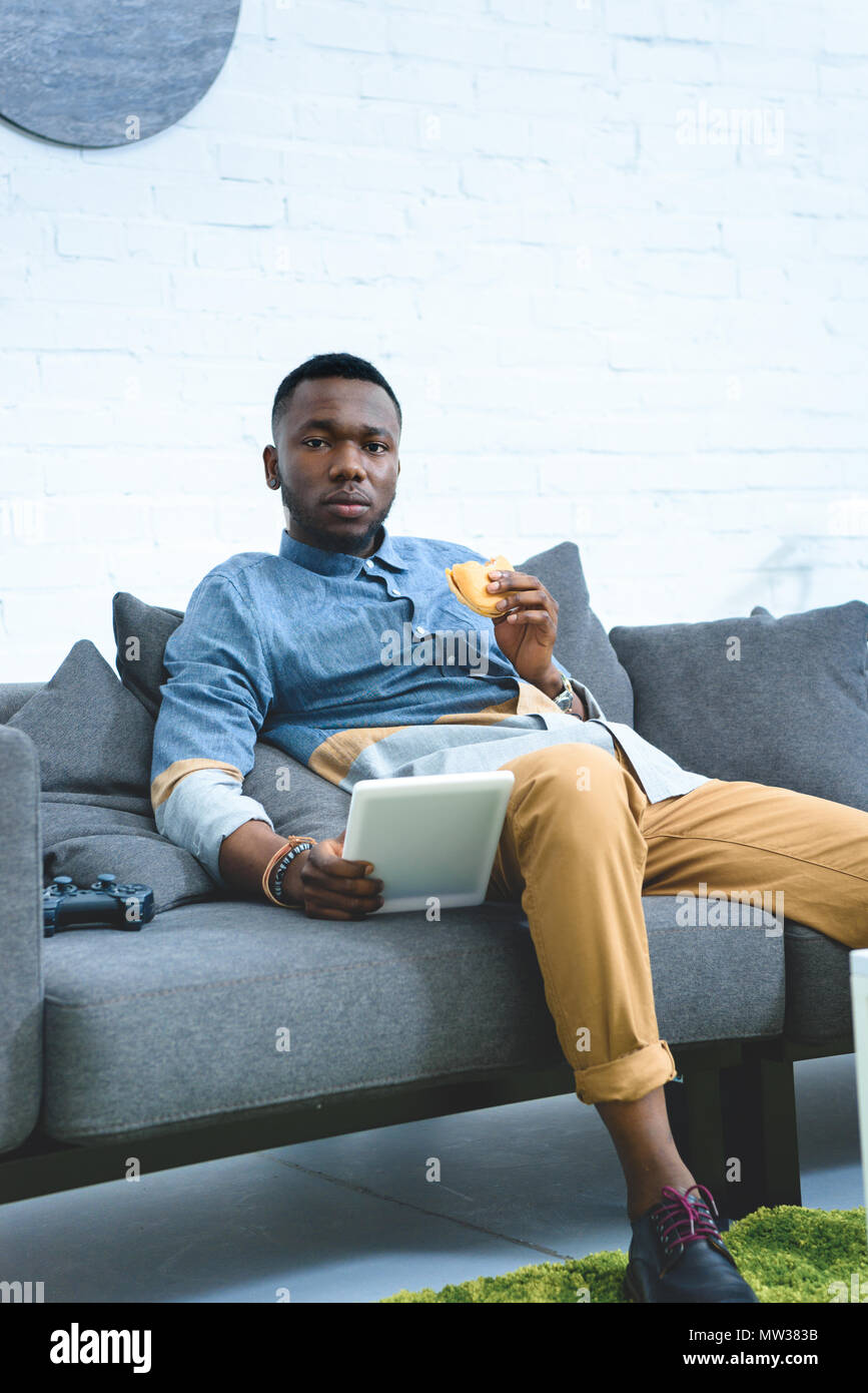 African american man holding tablet and eating hamburger Stock Photo ...