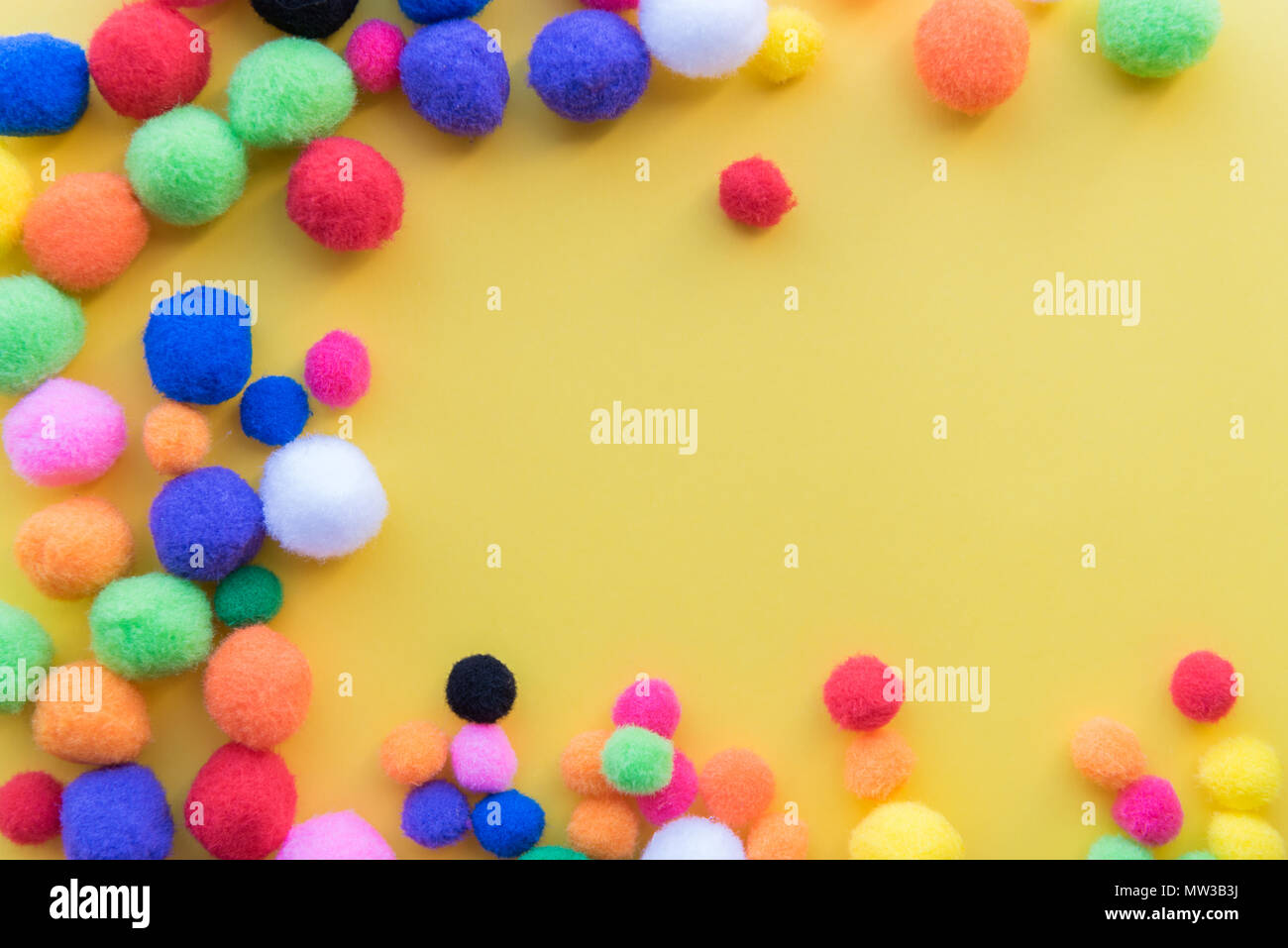 Flat lay arrangement of multi-colored craft pom-poms on solid yellow ...