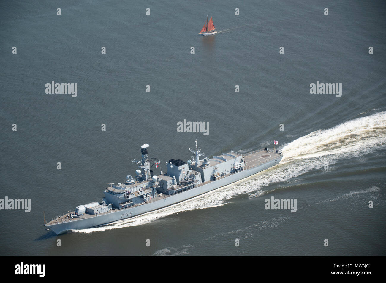Aerial photo of small red sailing boat racing Royal Navy Frigate Stock ...