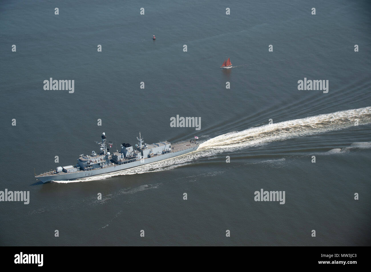 Aerial photo of small red sailing boat racing Royal Navy Frigate Stock ...