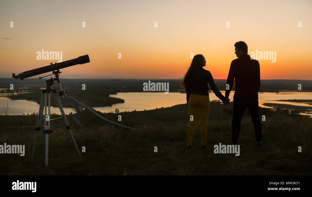 Telescope stands in front of couple holding hands on the hill at the ...