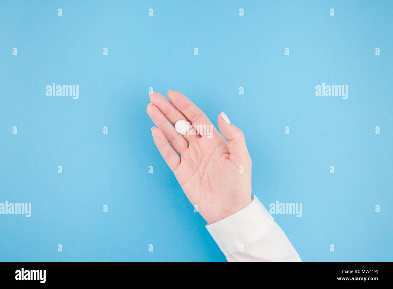Woman hand holding a white pill on pastel blue paper background with ...