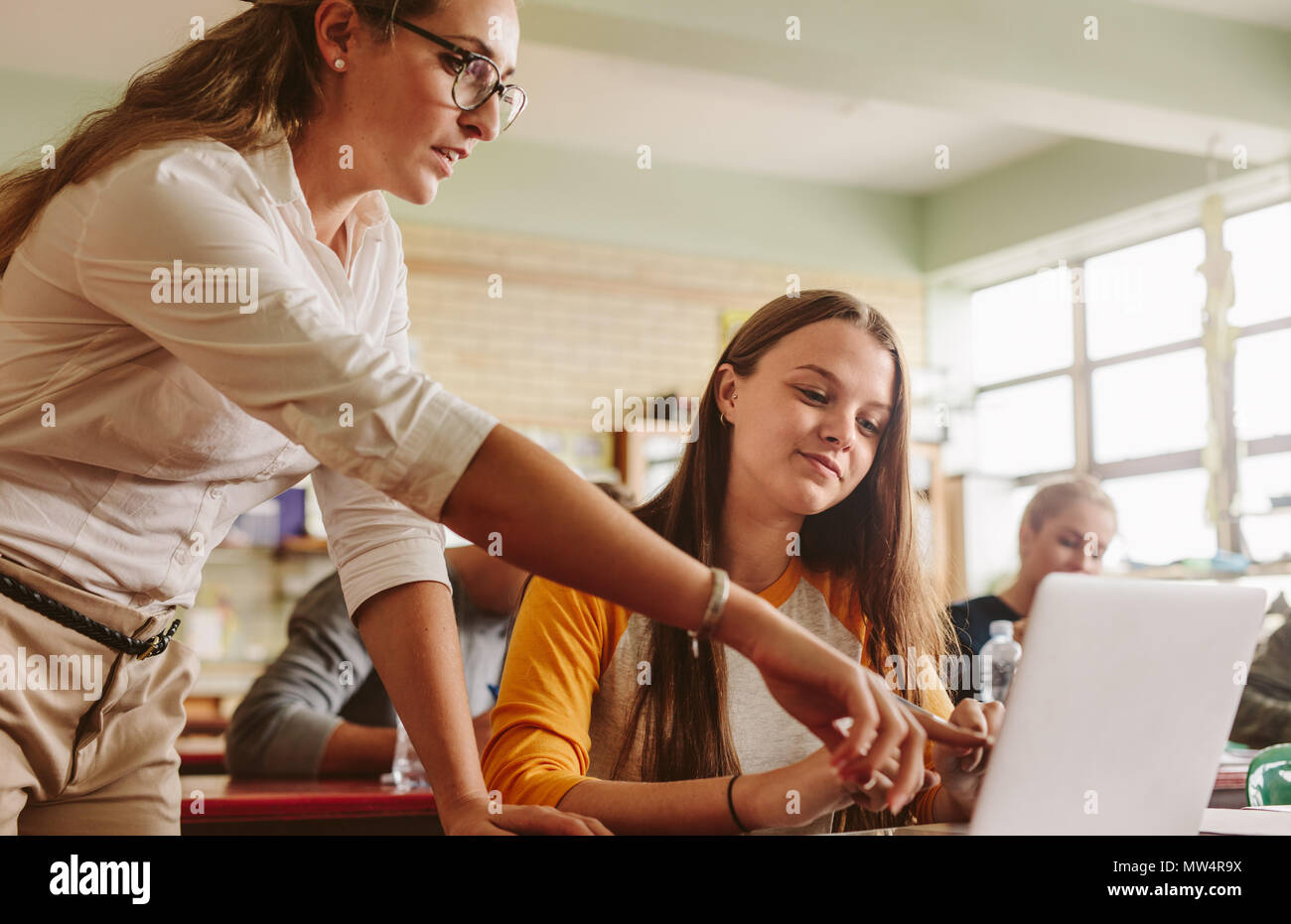 Teacher helping student in classroom. Lecturer pointing at laptop ...