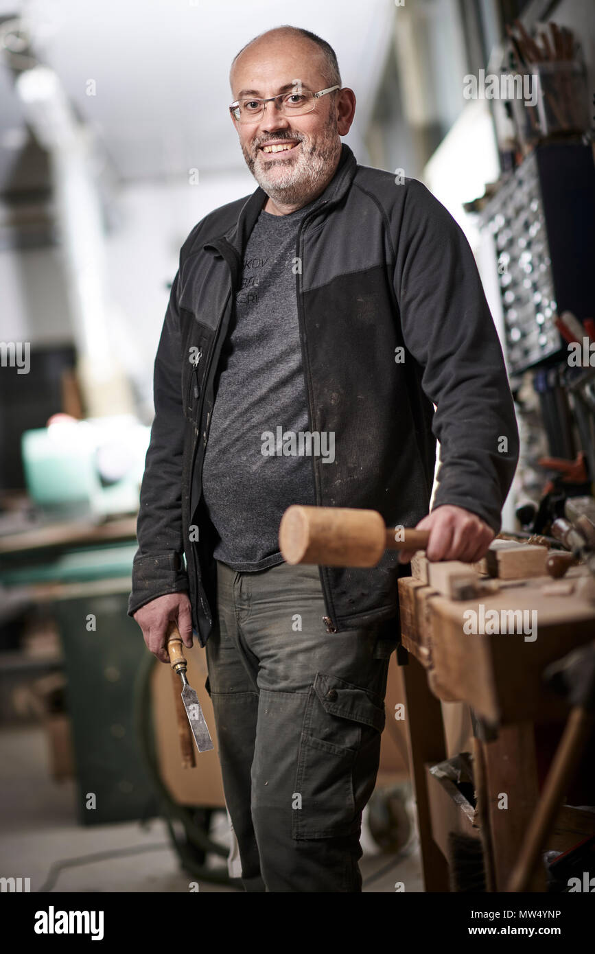 Cabinet maker in his workshop smiling while leaning against his bench ...