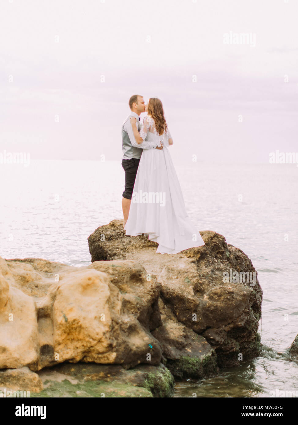 The kissing newlyweds standing on the cliff at the background of the ...