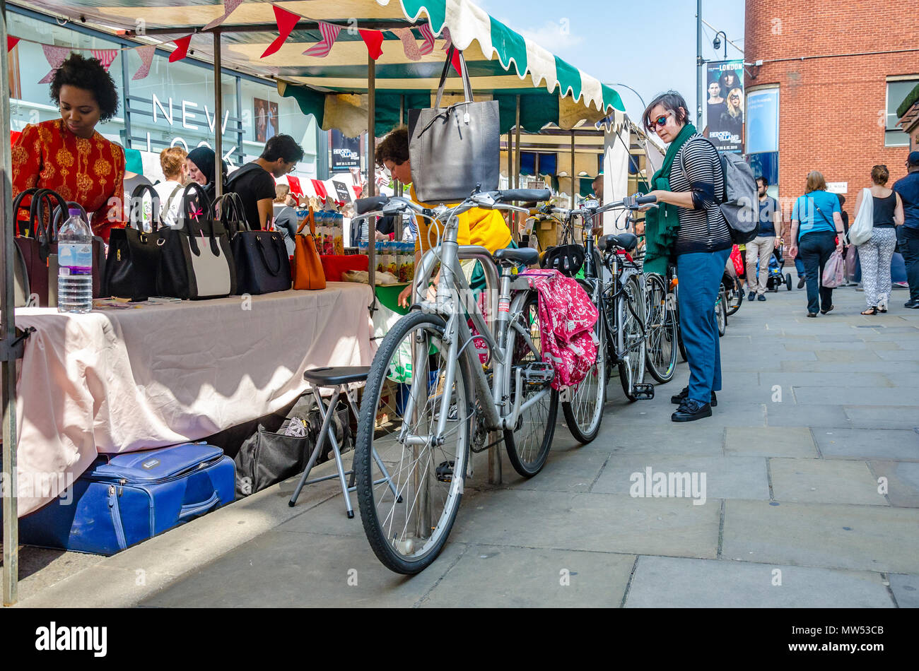 A lady parks her bicycle on a bike rack behind a handbag stall at a ...