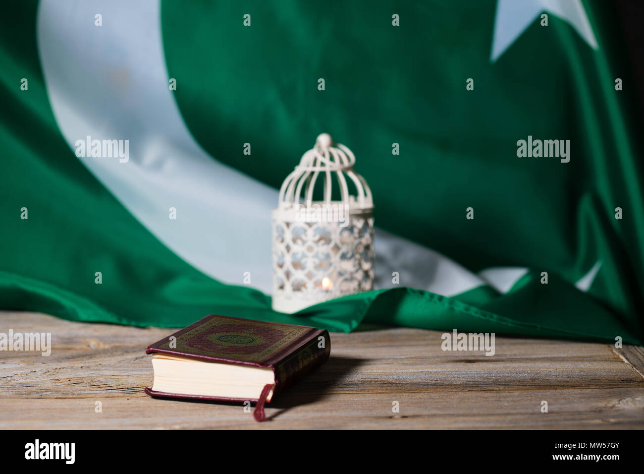 Sacred book of Quran on a wooden surface. Flag of Pakistan and candle ...