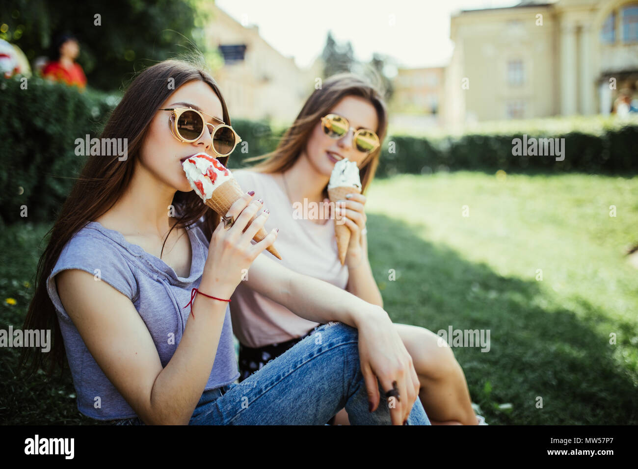 Portrait of two young women sitting on a curb eating ice cream in ...