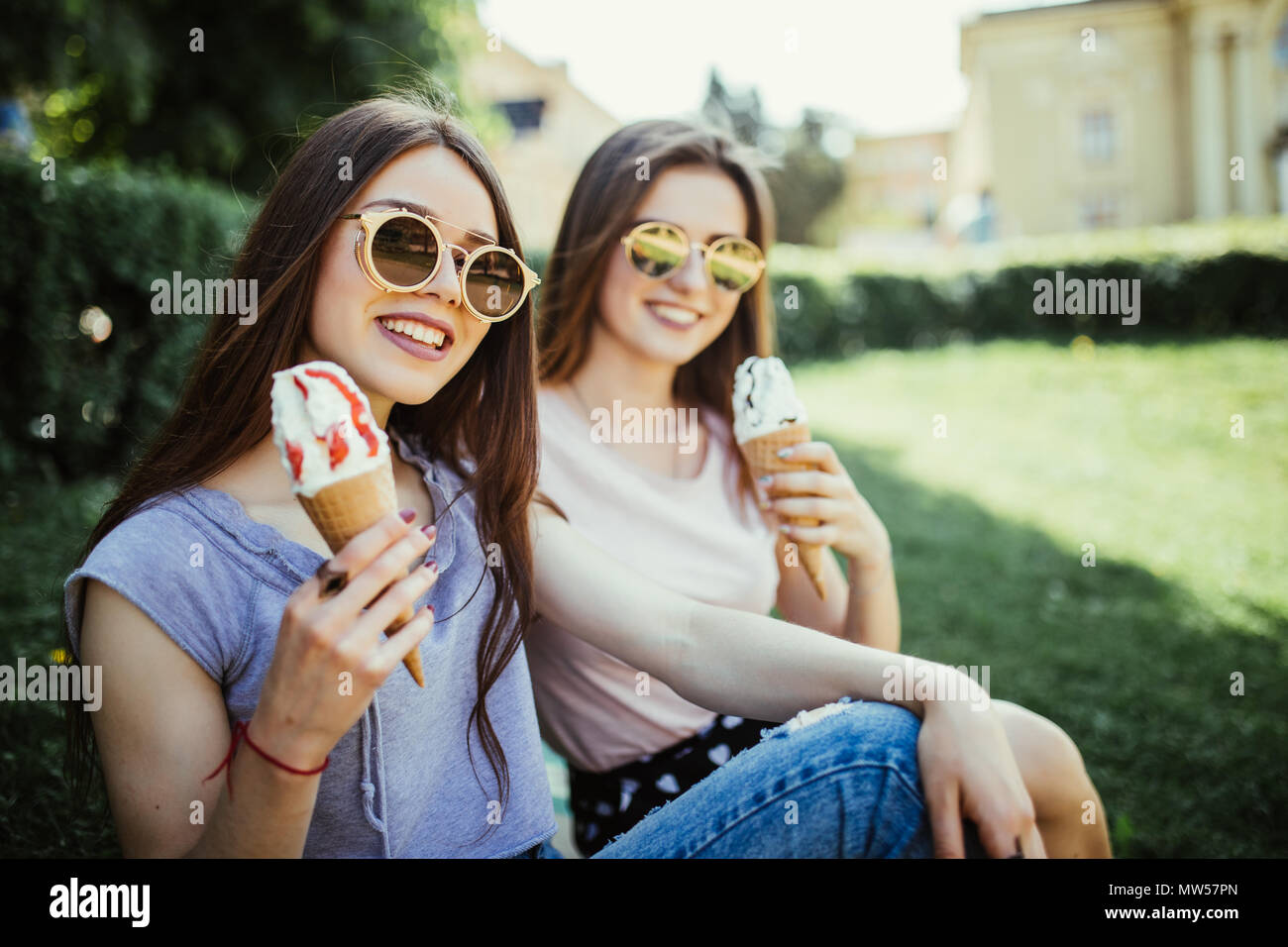 Young two women friends eat ice cream sitting on the grass in city ...