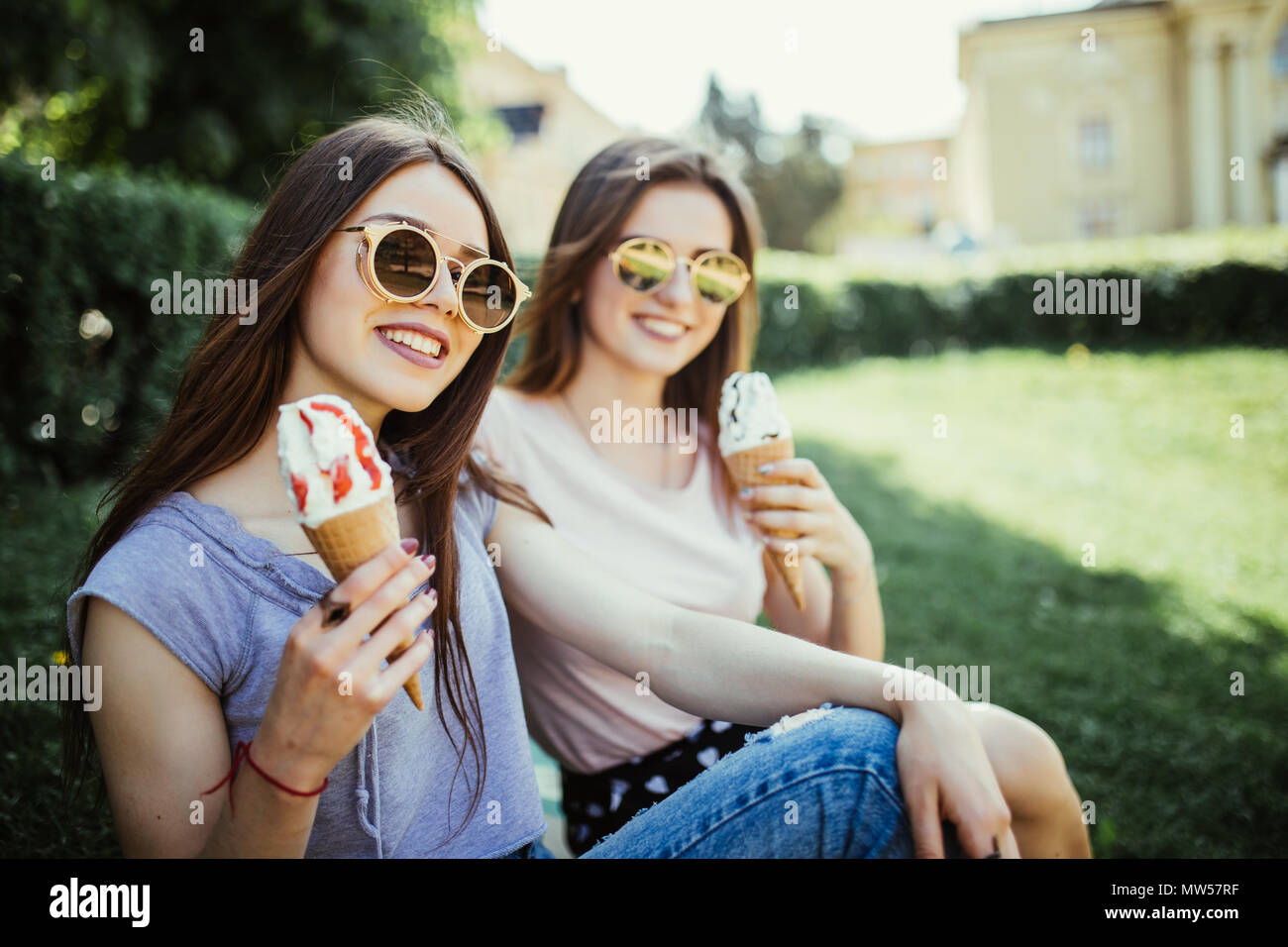 Portrait of two young women sitting on a curb eating ice cream in ...